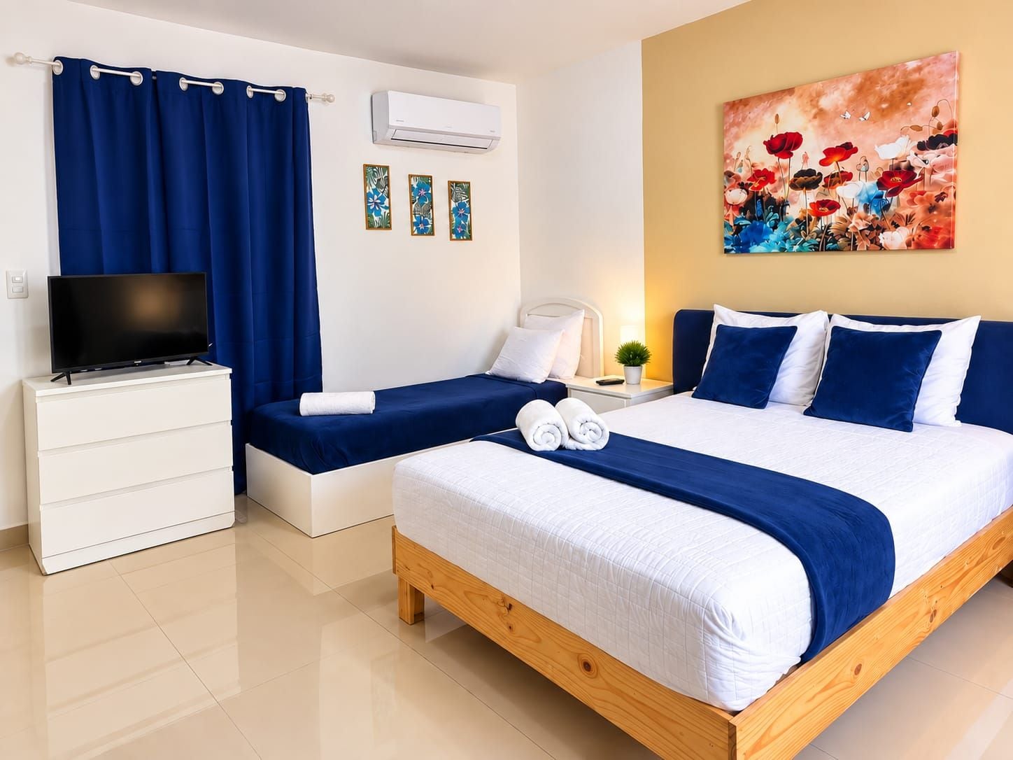 Quarto de hotel com cama, televisão, escrivaninha e um quadro na parede.