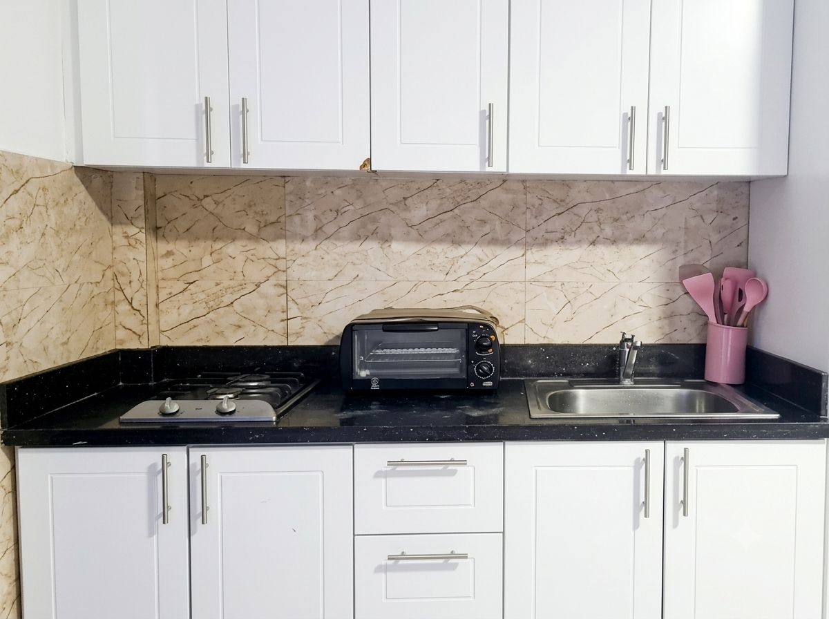 Cozinha com armários brancos, bancada preta, torradeira, pia e painel de backsplash de mármore.