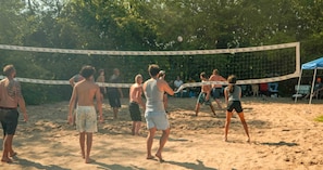 Um grupo de pessoas jogando vôlei de praia em uma quadra arenosa com uma rede no centro.