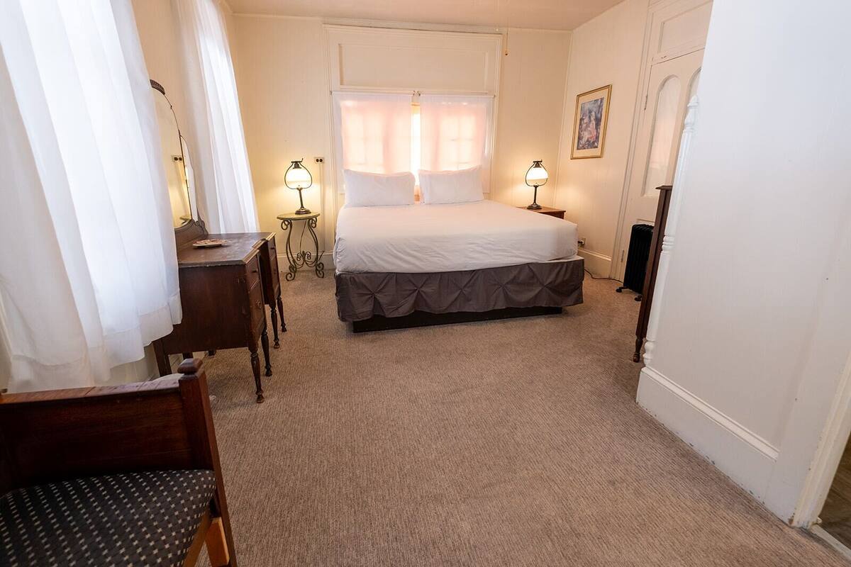 Quarto com cama, mesas de cabeceira, escrivaninha e cadeira.