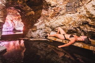 Uma pessoa deitada num banco em ambiente semelhante a uma gruta, com uma piscina.