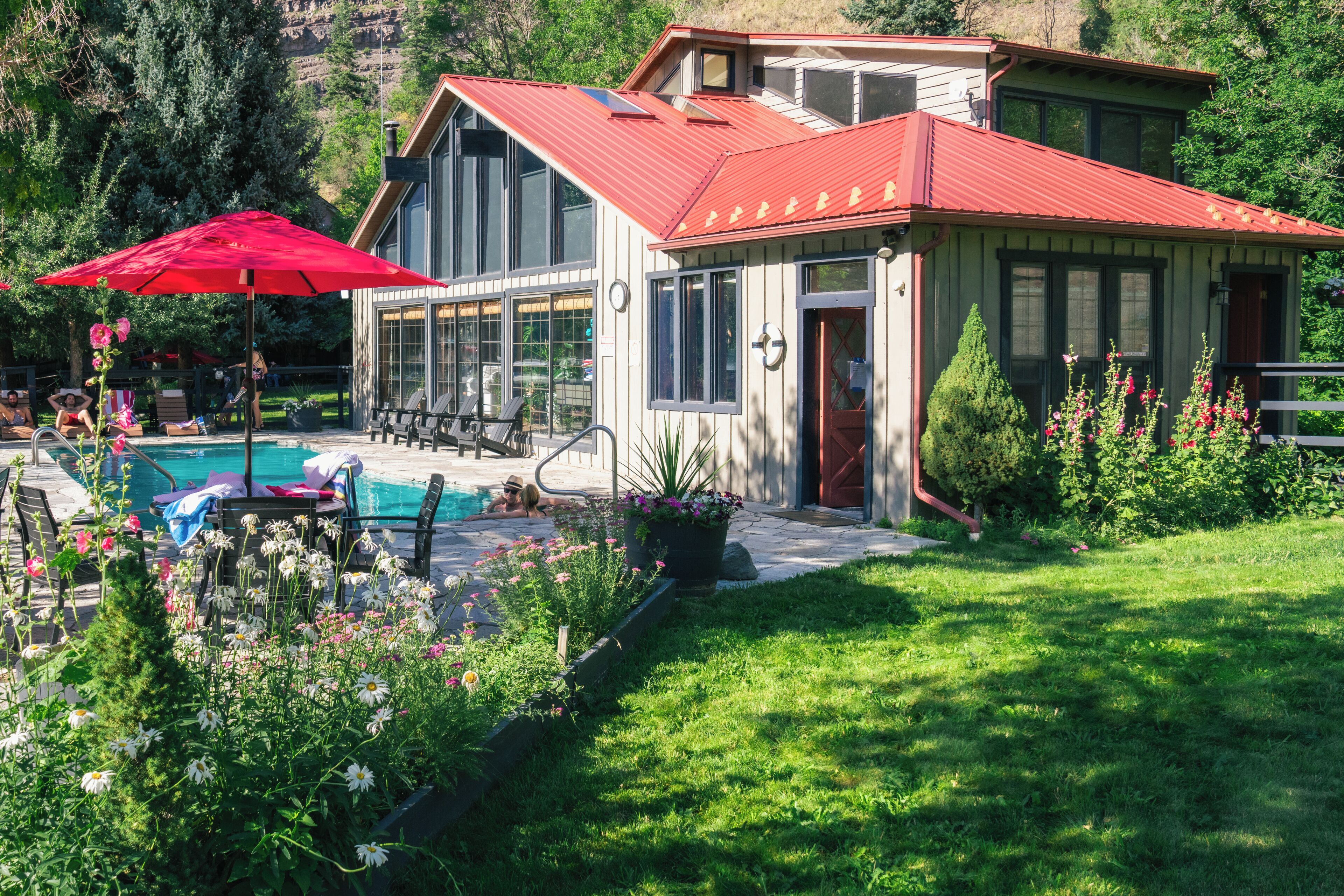 Uma casa com piscina, área de estar externa e um guarda-sol vermelho.
