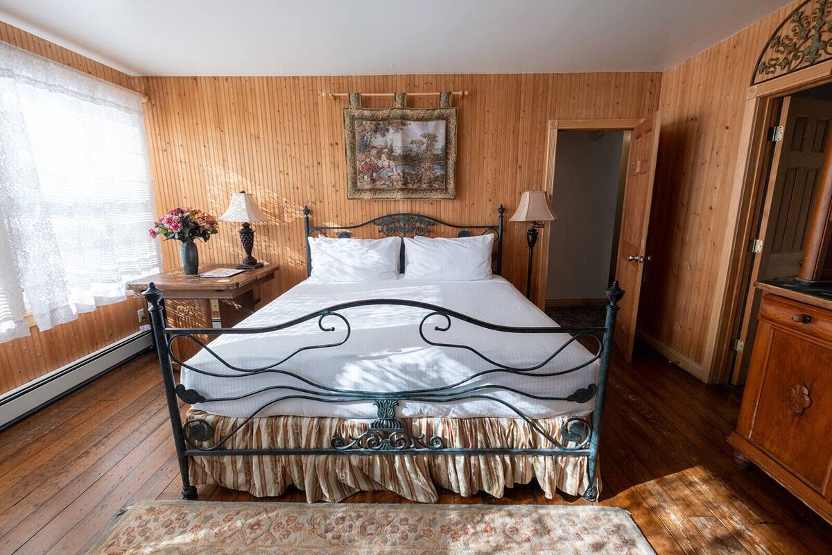 Quarto com painéis de madeira, uma cama, uma mesinha de cabeceira, um abajur e um quadro na parede.