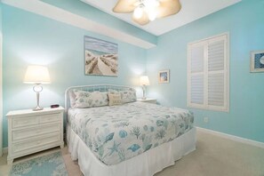 Um quarto com cama, duas mesas de cabeceira, um ventilador de teto, janela com persianas e um quadro na parede.