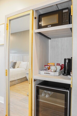 Quarto compacto com cama, micro-ondas, cafeteira e pequeno frigorífico.