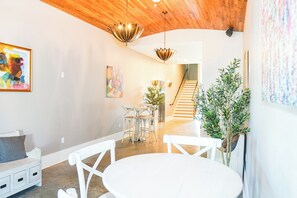 Um interior moderno com área de jantar, mobiliário branco, escada e obras de arte nas paredes.