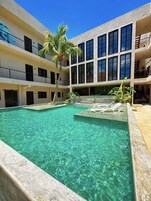 Um edifício com vários andares, piscina central, palmeiras e céu azul límpido.