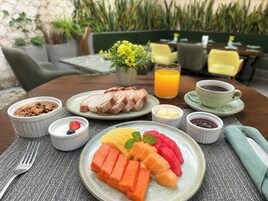 Uma mesa de café da manhã com uma tábua de frutas cortadas, um copo de suco de laranja e uma xícara de café.