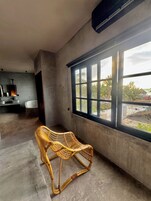 Um interior moderno com uma janela ampla, uma cadeira de vime e piso de concreto.