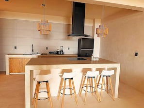 Uma cozinha moderna com ilha central, banquetas, luminárias pendentes e forno embutido.