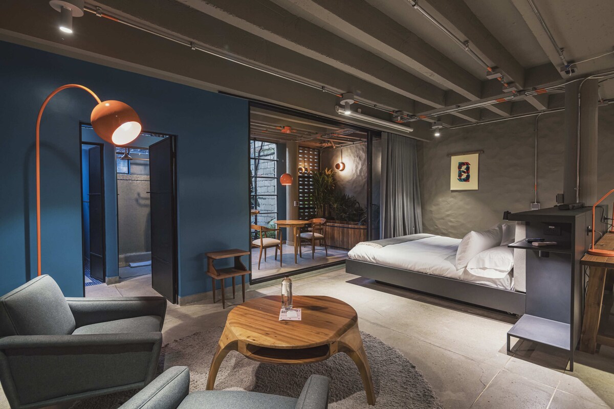 Quarto de hotel moderno com cama, área de estar e pequena mesa de jantar.