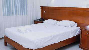 Quarto de hotel com cama de madeira, roupa de cama branca, mesa de cabeceira com telefone e uma banheira grande e branca.