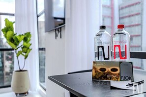 Quarto moderno com uma janela grande, uma planta em vaso e uma mesa com uma garrafa de água e um telefone.