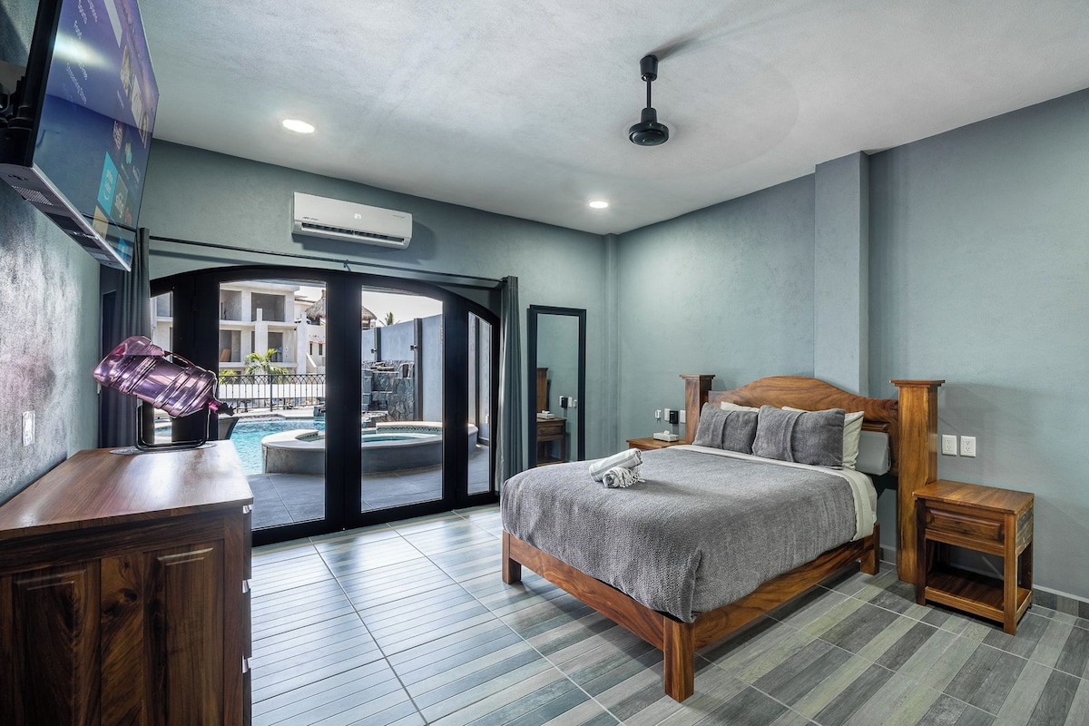 Quarto com cama, mesa de cabeceira e vista para uma piscina.