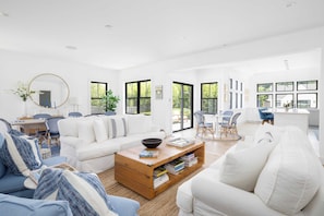 Uma sala de estar moderna com um sofá branco, uma mesa de centro e um canto de jantar com cadeiras e uma mesa.