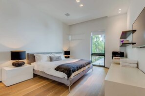 Quarto moderno com cama, mesas de cabeceira, escrivaninha e uma janela grande.