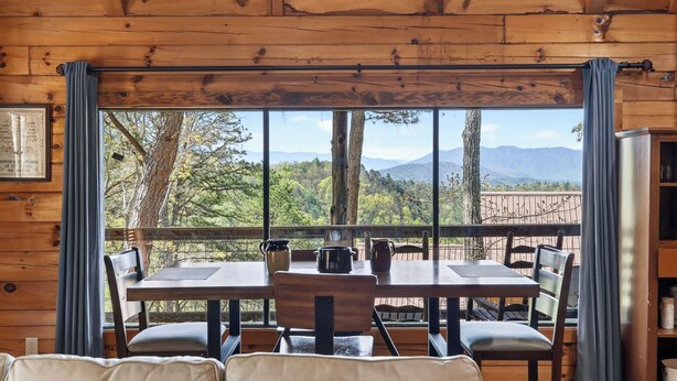 Uma cabana de madeira com área de refeições, incluindo mesa, cadeiras e vista para montanhas.