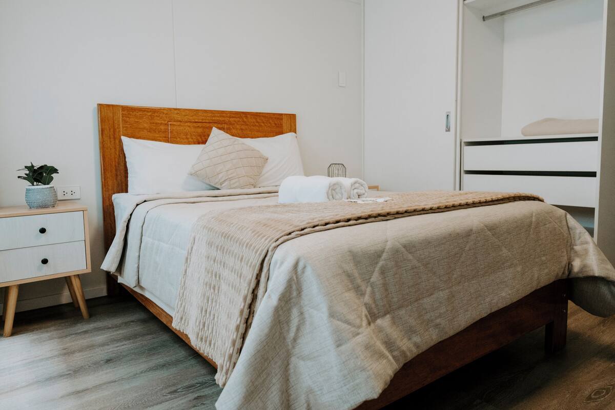 Quarto com cama de madeira, mesa de cabeceira com abajur e guarda-roupa embutido.