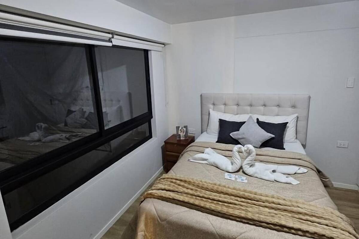 Quarto com cama, janela, mesa de cabeceira e painel de cabeceira.