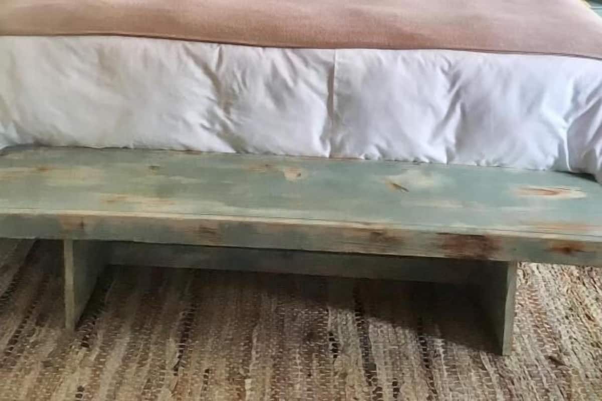 Uma cama com um banco, duas luminárias de cabeceira e uma cabeceira com persianas.
