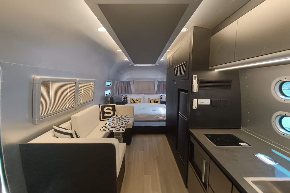 Interior compacto de um veículo recreativo, com cozinha compacta, cama com travesseiro escrito 'Hello' e um pequeno espaço de estar.