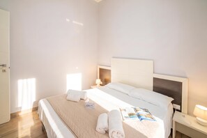 Quarto de hotel com cama, mesa de cabeceira, abajur e porta.