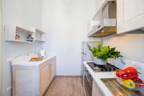 Cozinha compacta com bancada branca, fogão e uma pia pequena. Armários de madeira e parede branca.