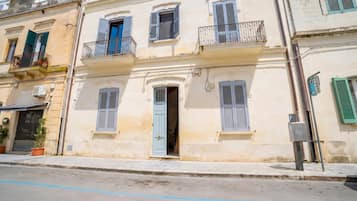 Fileira de edifícios em estilo mediterrâneo tradicional, com varandas, céu azul límpido e rua pavimentada.