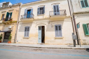Fileira de edifícios em estilo mediterrâneo tradicional, com varandas, céu azul límpido e rua pavimentada.