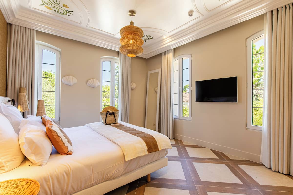 Um quarto com uma cama grande, uma televisão na parede e uma janela com cortinas.