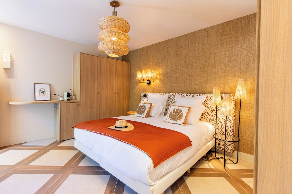 Quarto de hotel com cama, guarda-roupa, mesa de cabeceira, abajur e luminária na parede.