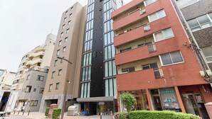 Edifício de vários andares com fachada de vidro central, diversas varandas e entrada no nível da rua.