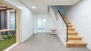 Um corredor com escadas, uma porta que dá para uma varanda e uma pequena mesa com cadeiras.