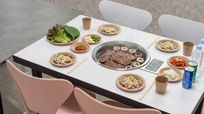 Uma mesa de jantar com uma churrasqueira, diversos pratos e uma garrafa de água.