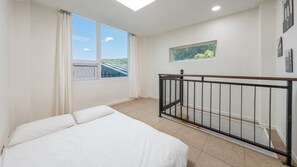 Um quarto com uma cama, uma janela com vista para uma ponte, uma pequena janela com vista para árvores e uma escada com corrimão.