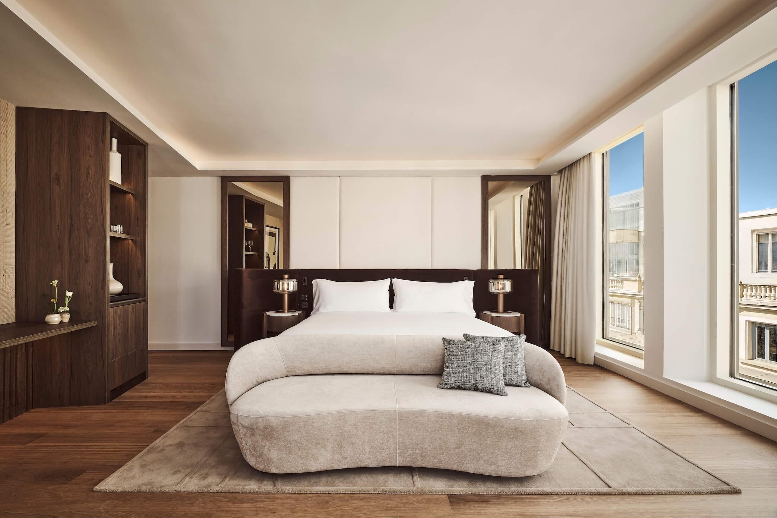 Quarto moderno com cama grande, roupeiro embutido, abajures e vista para a cidade.