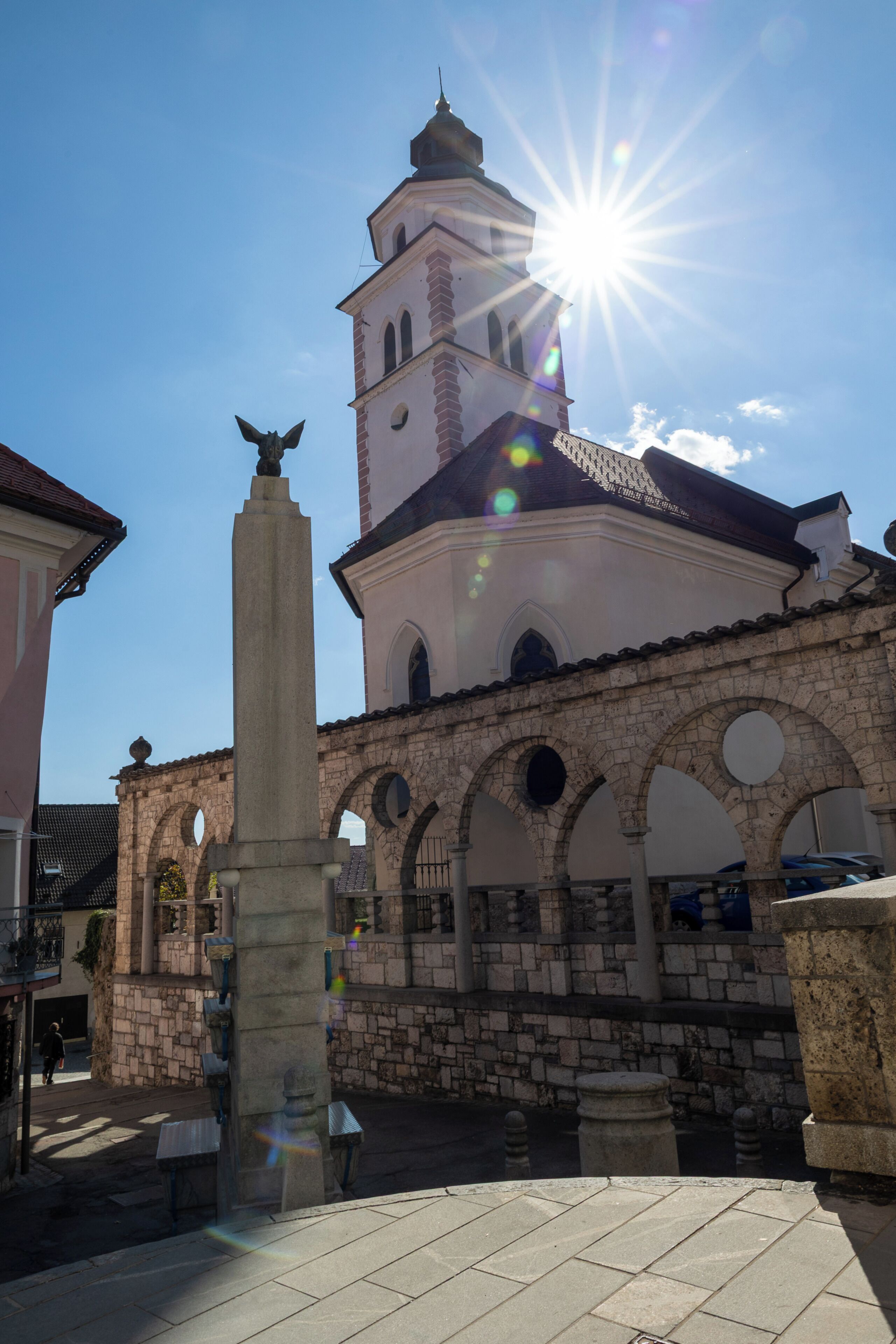 Um edifício histórico com uma torre imponente, um monumento central e uma série de arcos.