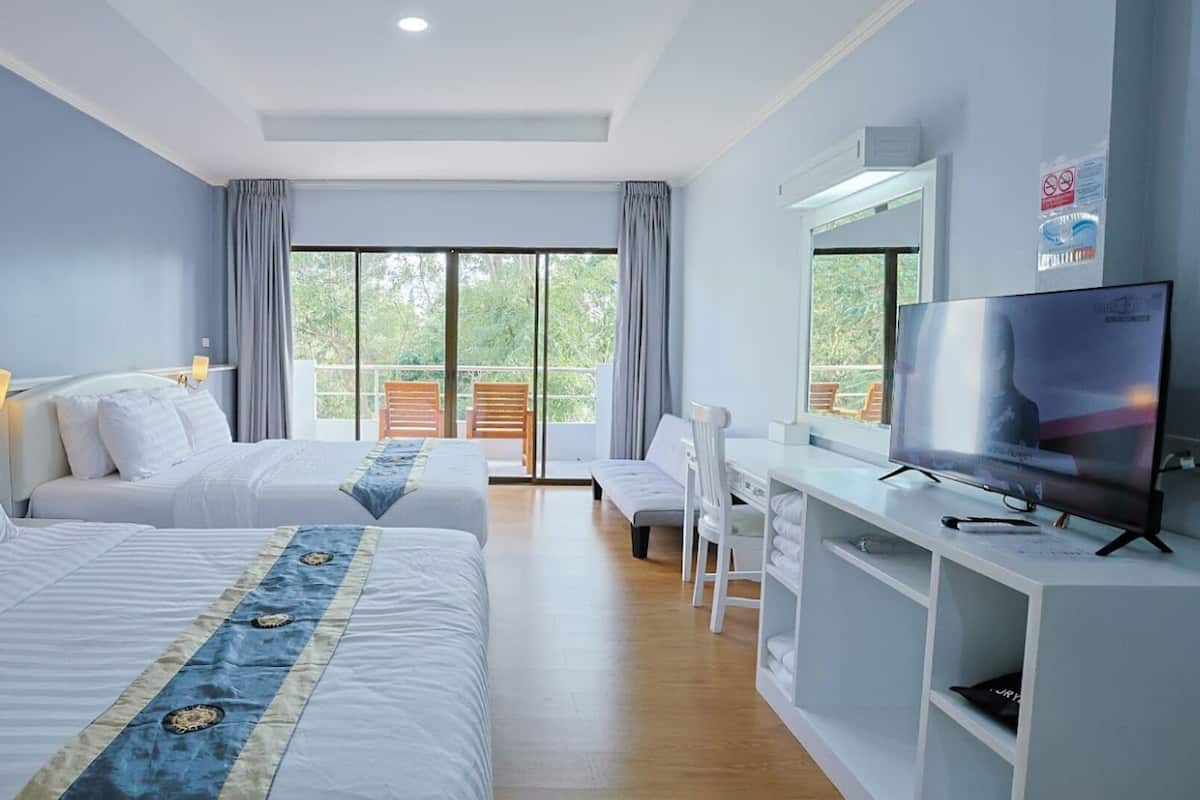 Quarto de hotel com duas camas, televisão, escrivaninha e varanda com cadeiras.