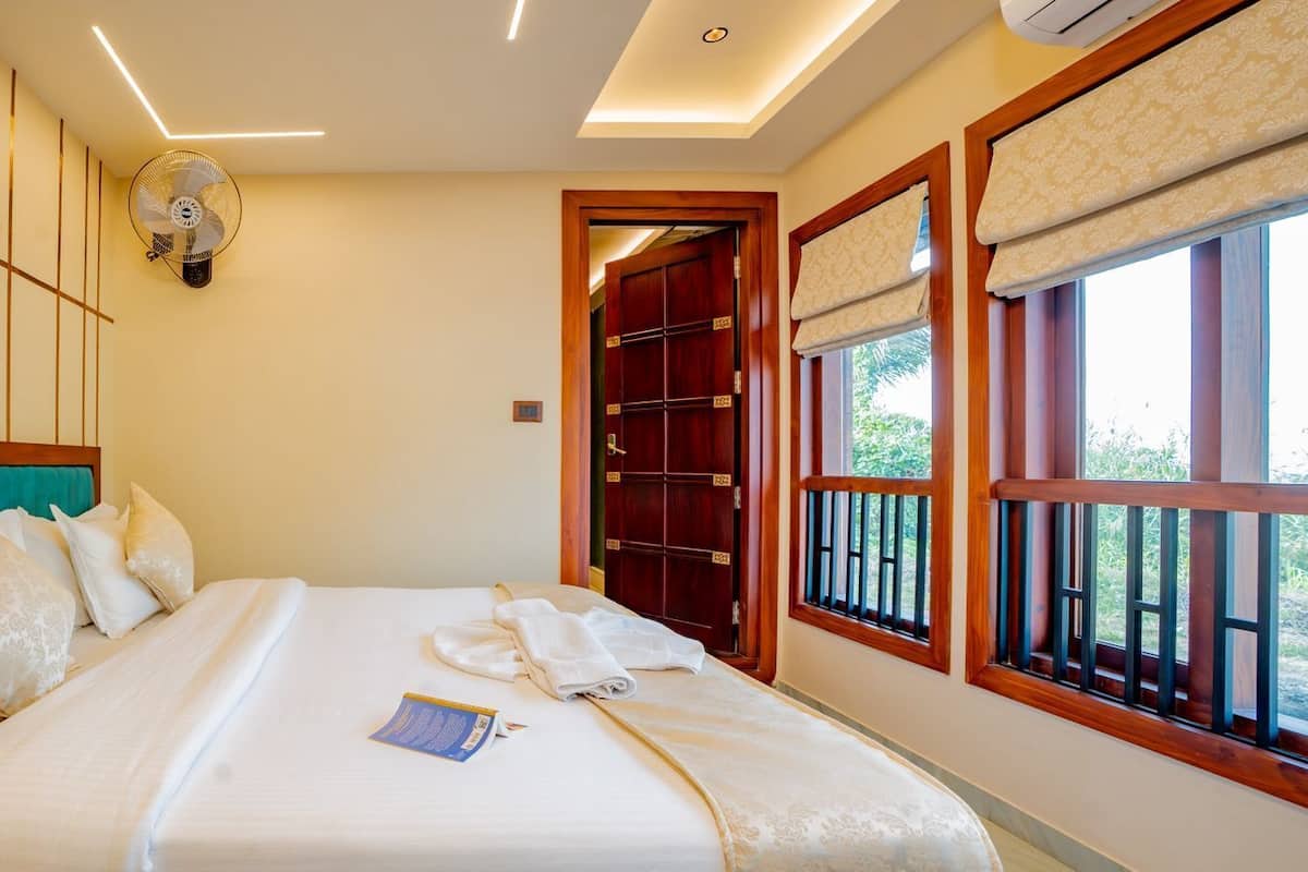 Quarto de hotel com cama, ventoinha, janela com vista e porta que dá para outro quarto.
