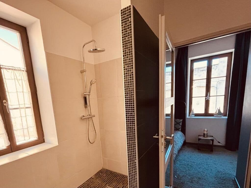 Casa de banho com chuveiro, janela e vista para um quarto.