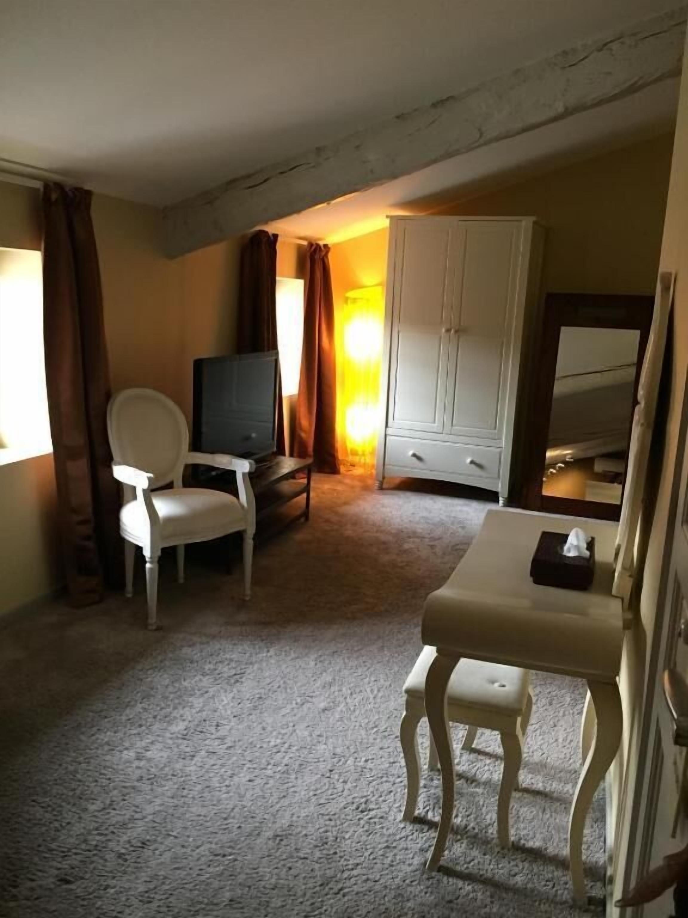 Quarto com televisão, um armário branco, uma cadeira branca e uma pequena mesa.