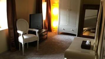 Quarto com televisão, um armário branco, uma cadeira branca e uma pequena mesa.