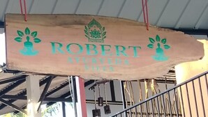 Uma placa de madeira com o nome 'ROBERT AYURVEDA VILLA' pendurado em uma estrutura de metal.