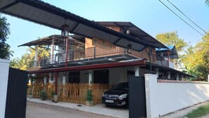 Uma casa de dois andares com uma varanda, um carro estacionado na frente e um portão.