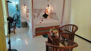 Quarto com uma cama de dossel, uma cadeira de madeira, uma mesinha com um vaso e um ventilador.