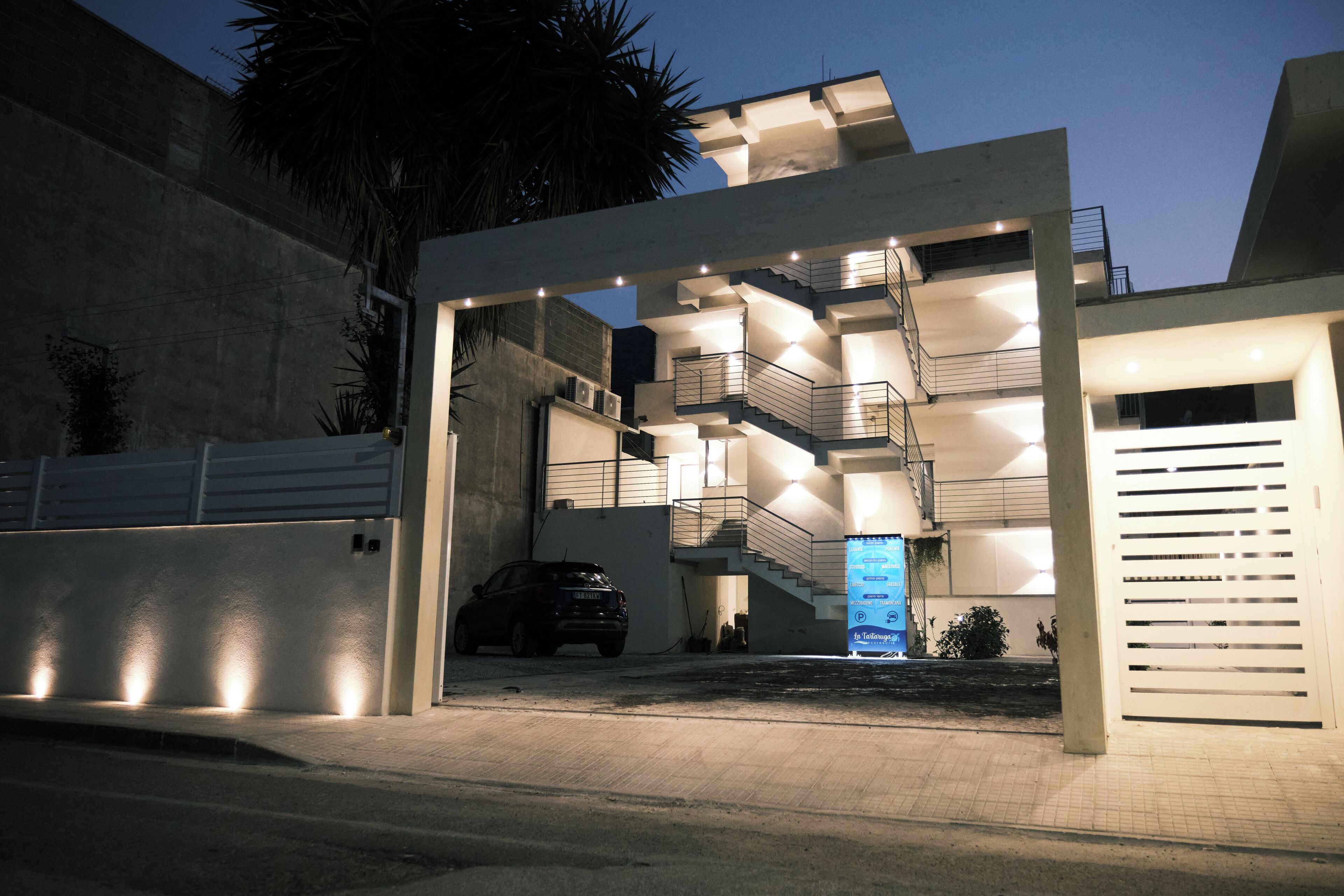 Um edifício moderno com vários andares, uma escadaria e um carro estacionado em frente.