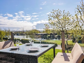 Uma área de refeições ao ar livre com uma mesa posta para dois, com vista para a água e um jardim.