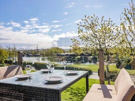 Uma área de refeições ao ar livre com uma mesa posta para dois, com vista para a água e um jardim.