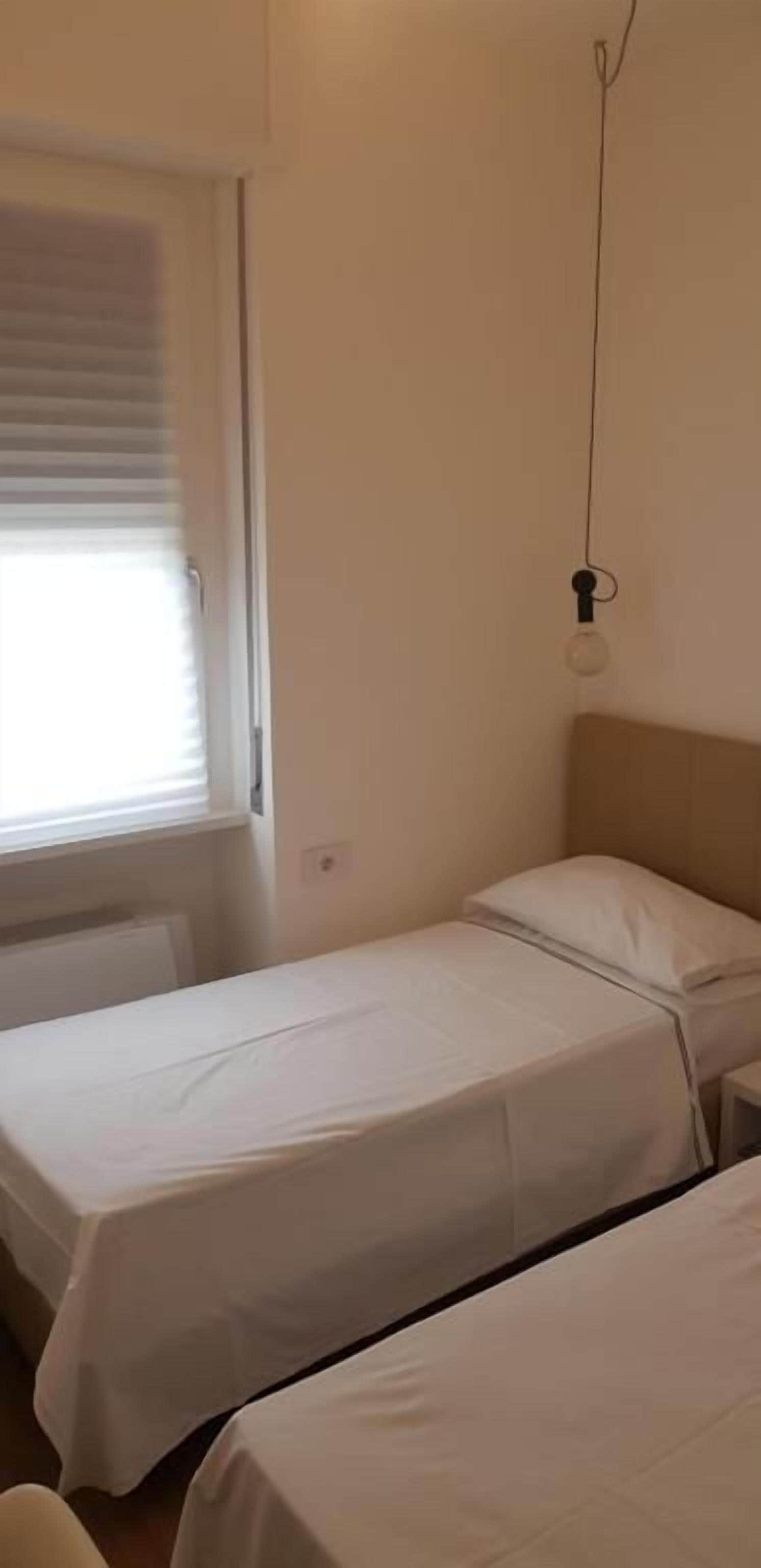 Quarto pequeno com uma cama de solteiro, janela, mesa de cabeceira e luminária pendente.