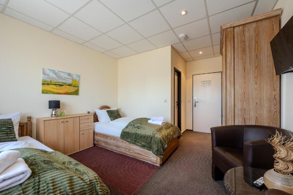 Quarto de hotel com duas camas, um guarda-roupa de madeira, uma televisão e um quadro na parede.